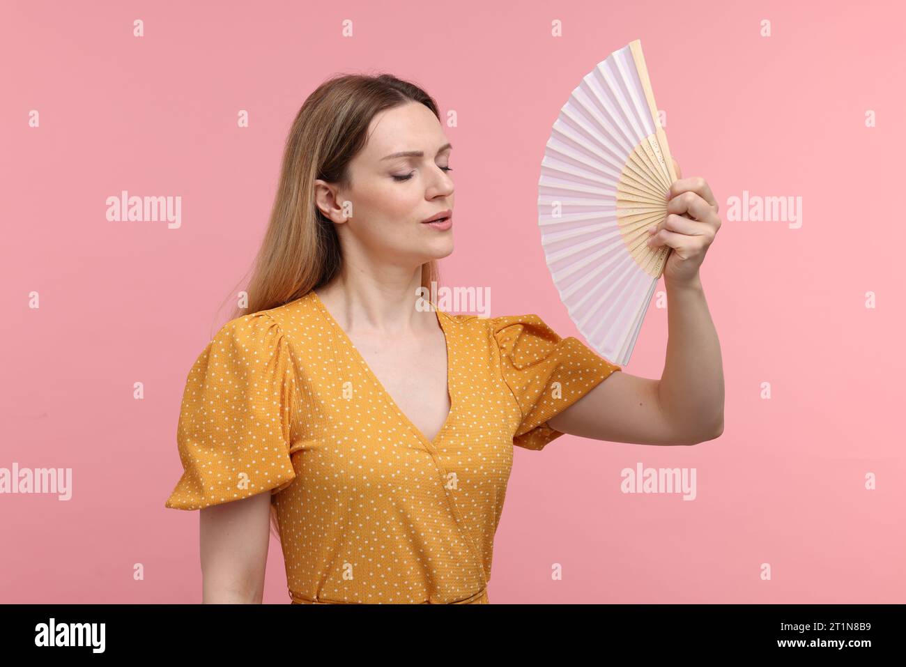 Beautiful woman waving yellow hand fan to cool herself on pink ...
