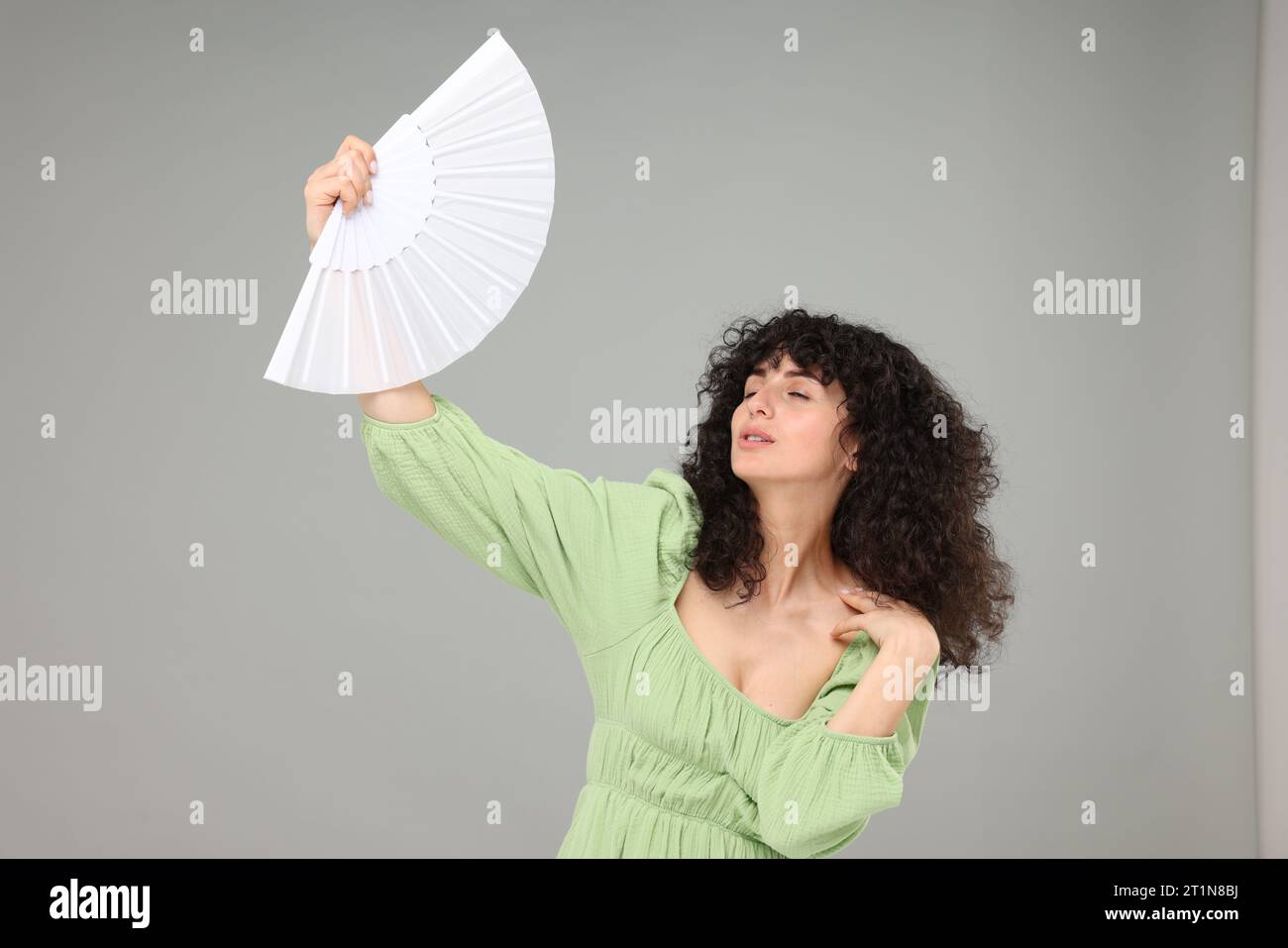 Woman with hand fan suffering from heat on light grey background Stock ...
