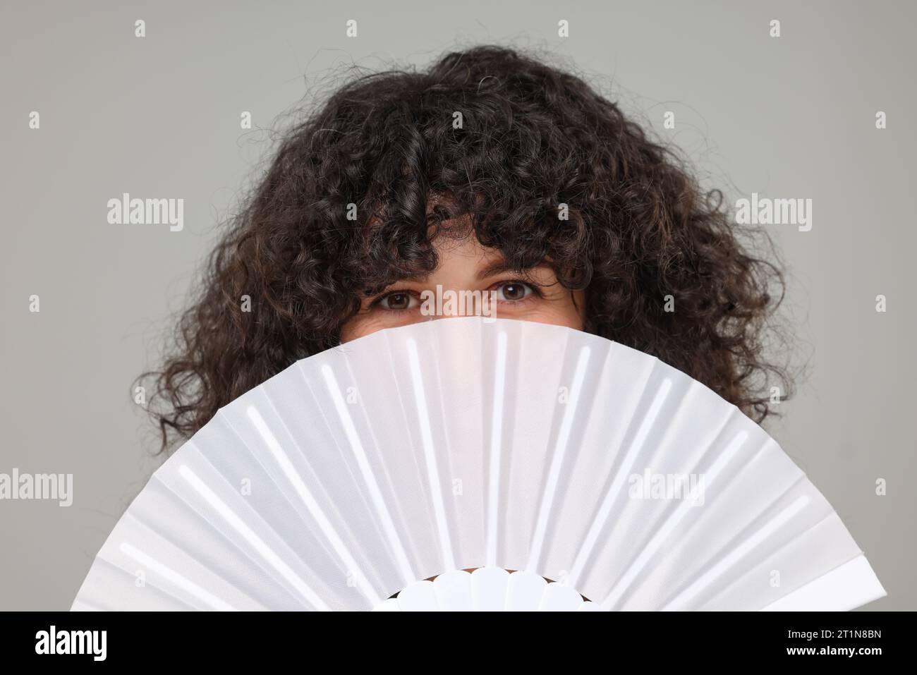 Woman hiding her face behind hand fan on light grey background Stock ...