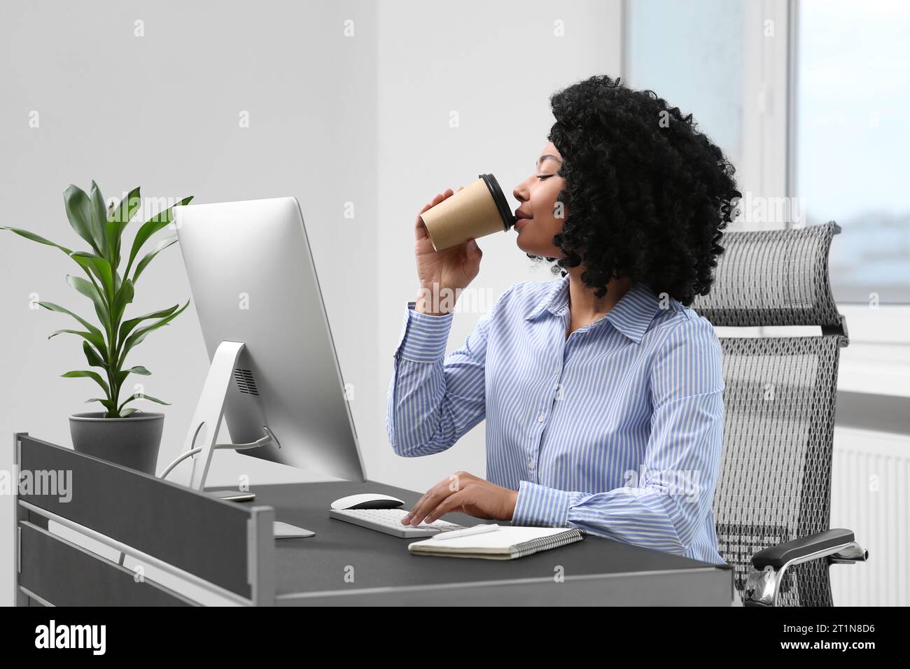 Young woman drinking coffee while working on computer in office Stock ...