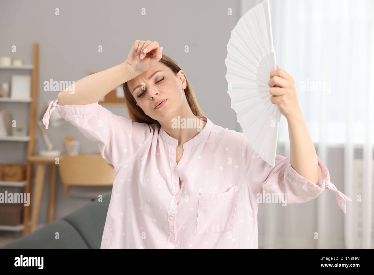 Woman waving white hand fan to cool herself at home Stock Photo - Alamy