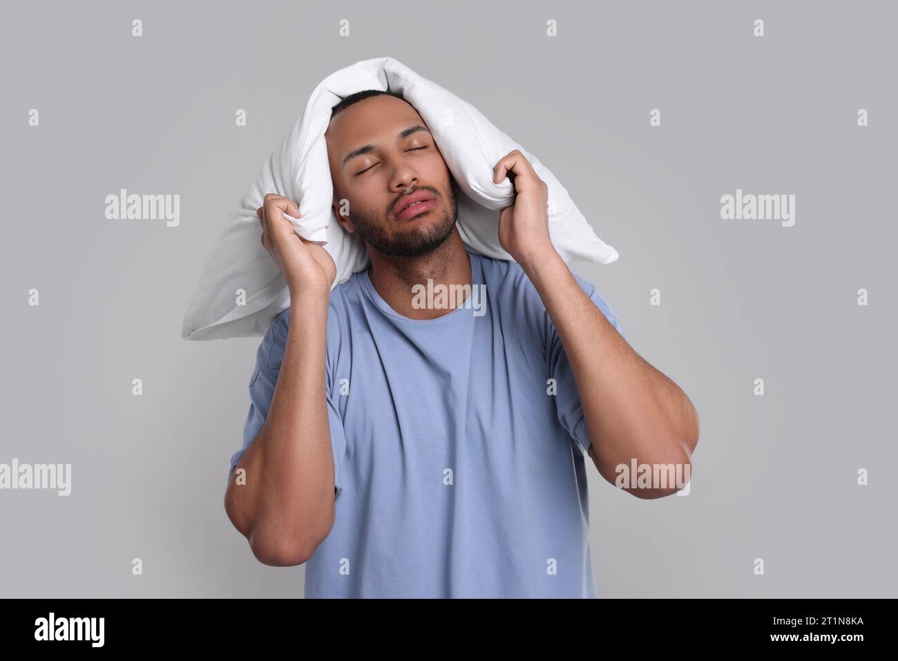 Tired man covering ears with pillow on light grey background. Insomnia ...