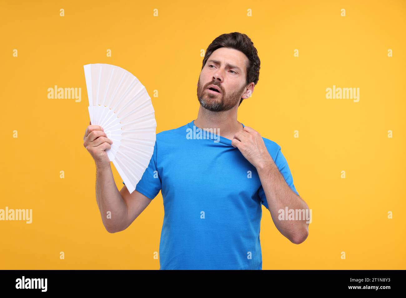 Unhappy man with hand fan suffering from heat on orange background ...