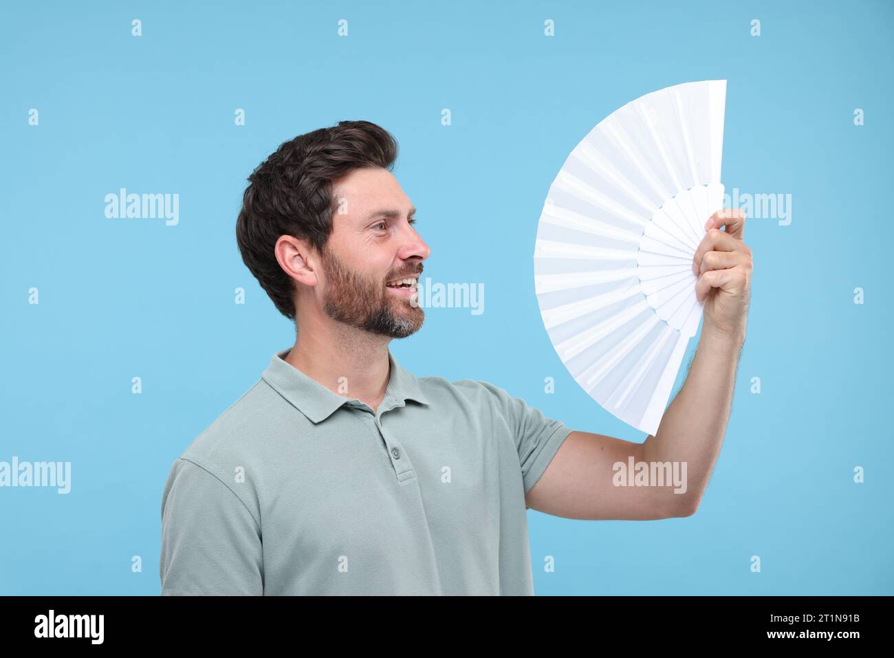 Happy man holding hand fan on light blue background Stock Photo - Alamy