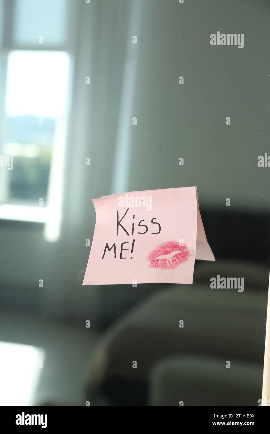 Sticky note with phrase Kiss Me and lipstick mark attached to mirror in ...