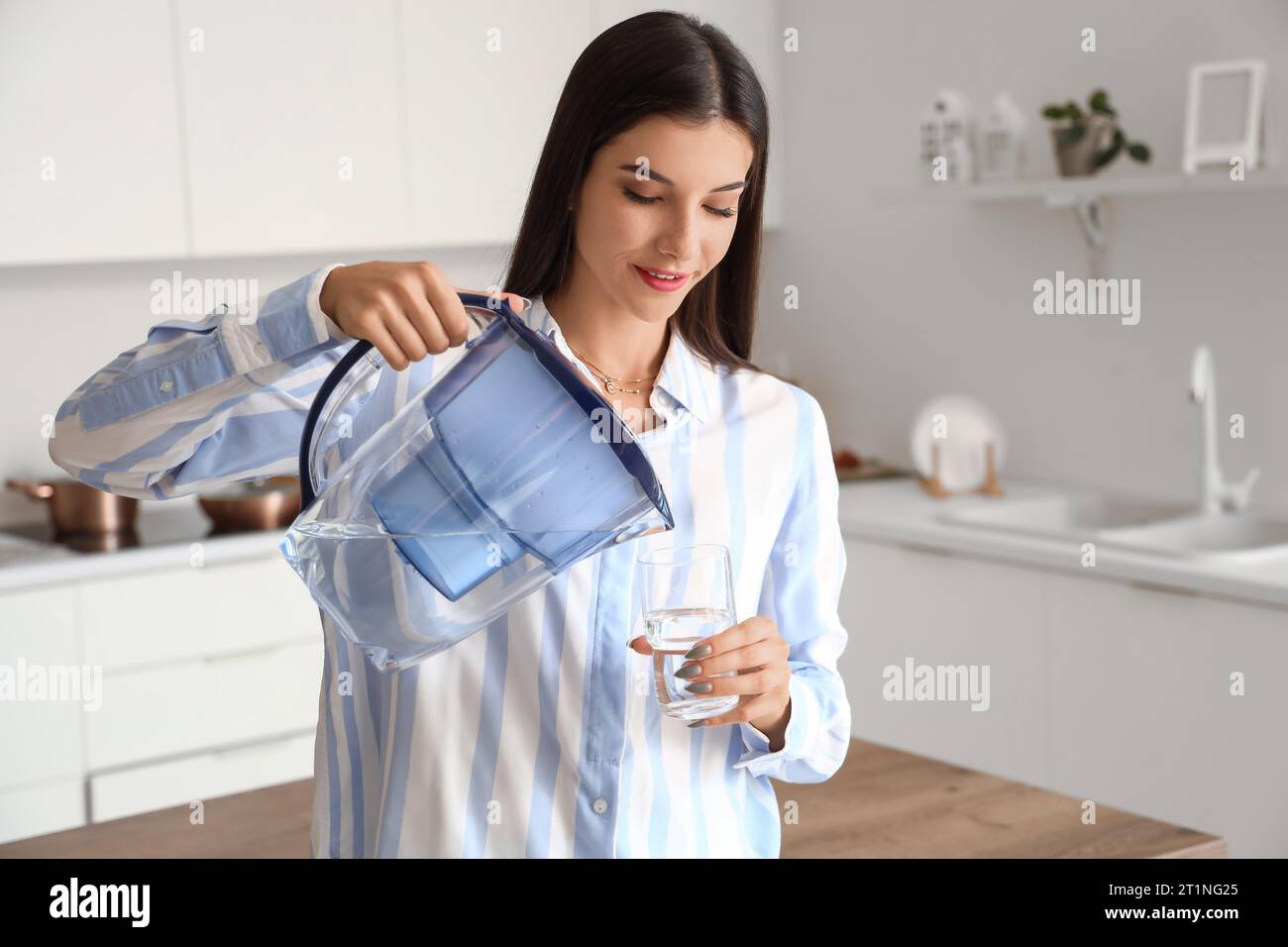 Young woman pouring water from filter jug into glass in kitchen Stock Photo - Alamy
