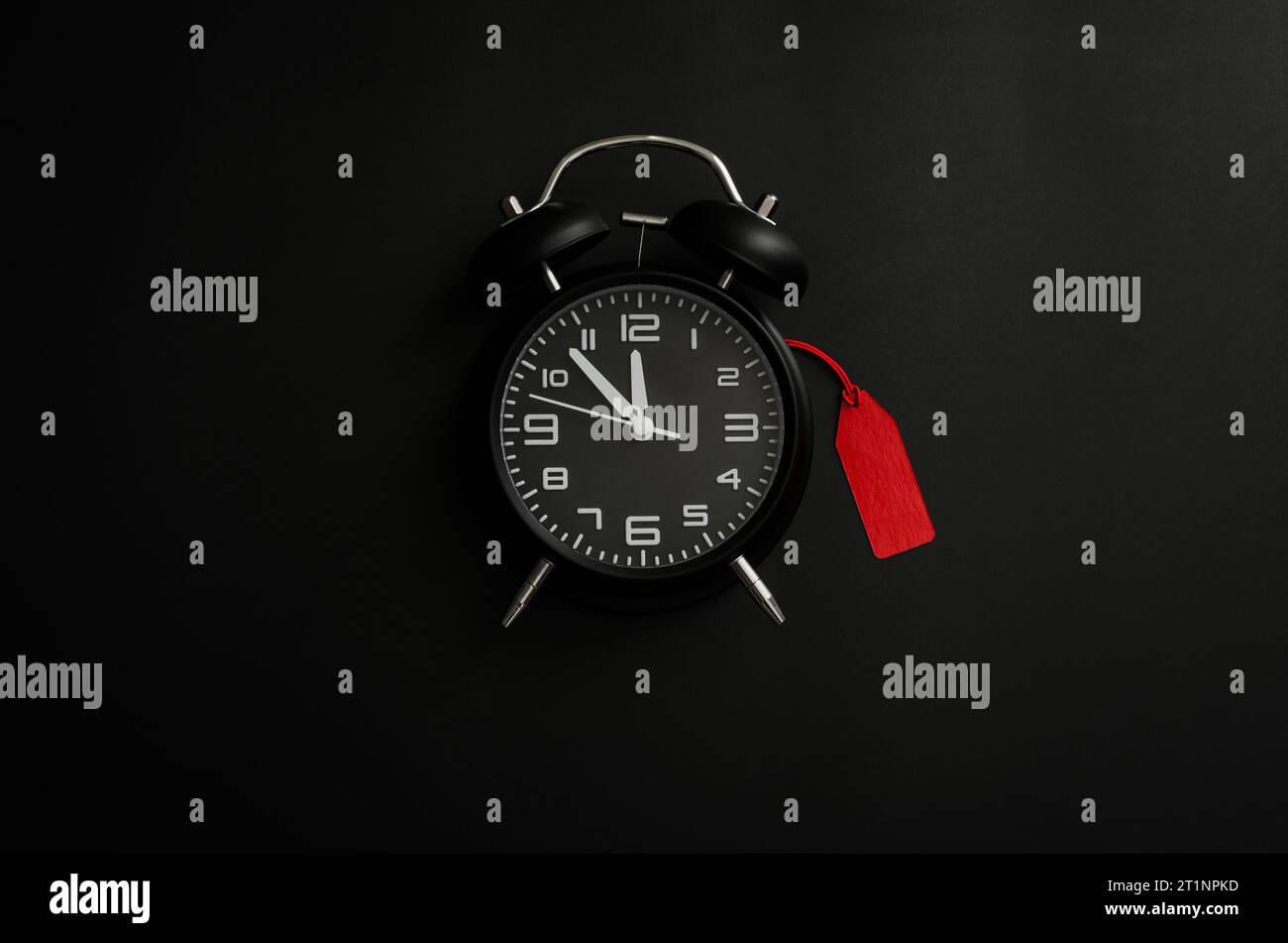 Black alarm clock with red blank price tag on black background for ...
