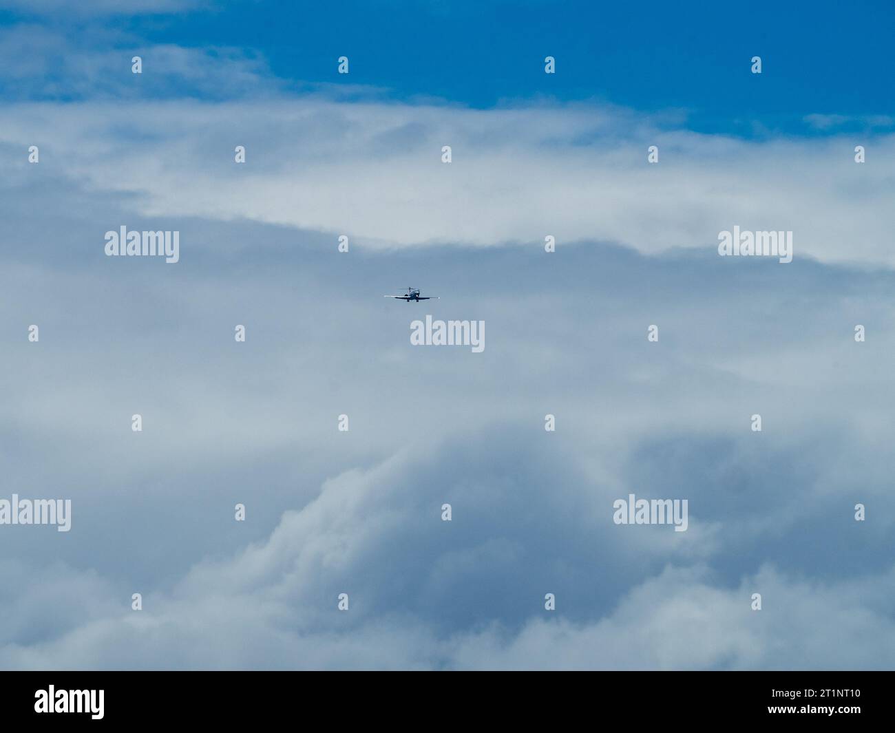 A distant plane flying through a sea of white clouds with blue sky ...