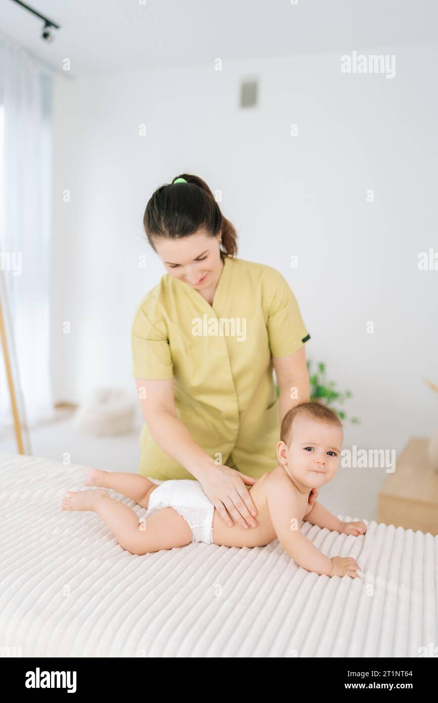 Vertical portrait of loving mother massaging little baby. Front view of ...