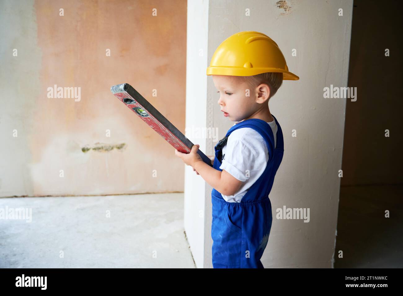Child checking wall surface with spirit level in apartment. Kid in work ...