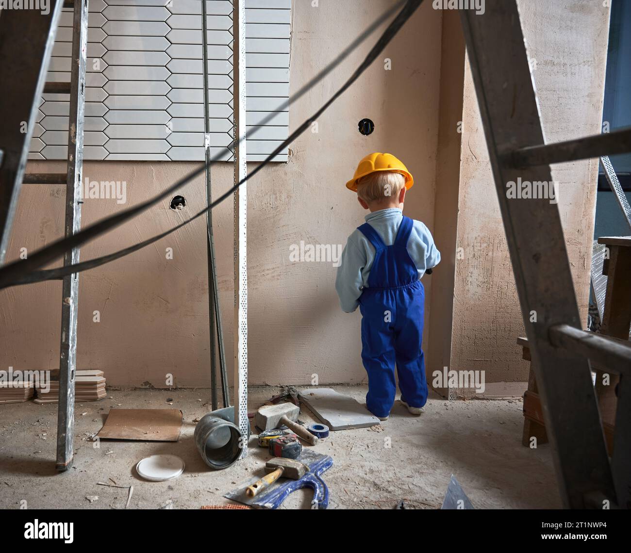Kid construction worker painting wall with brush in apartment under ...