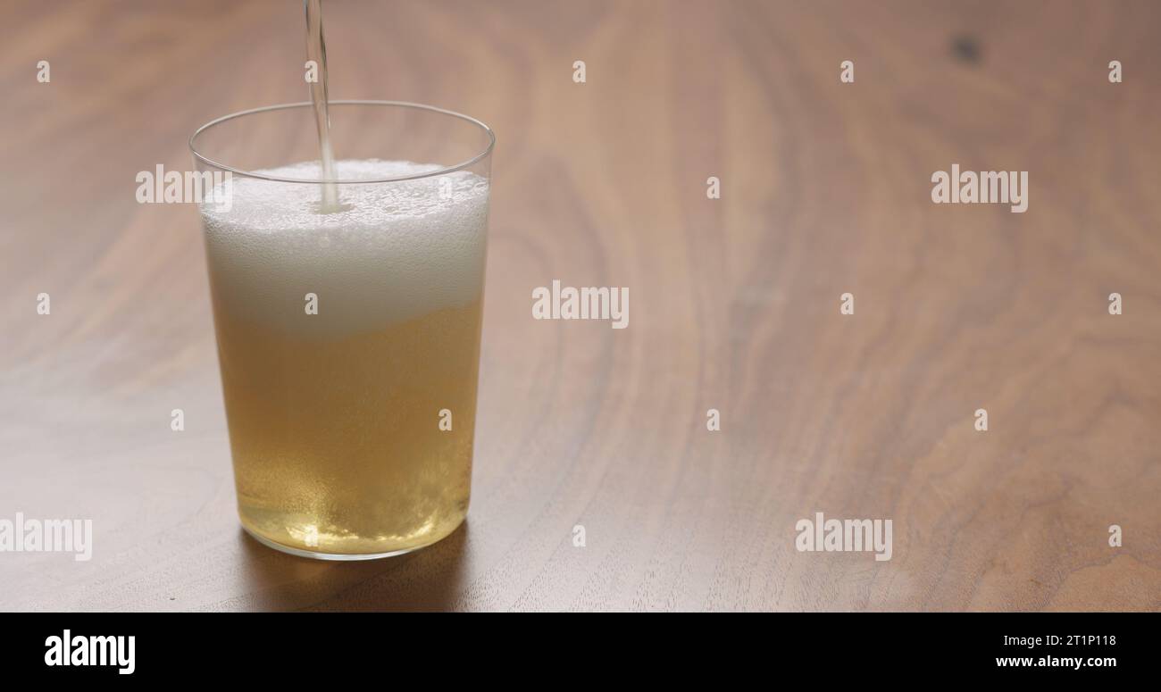 Pour light lager beer in thin wall glass on a wood table with copy ...