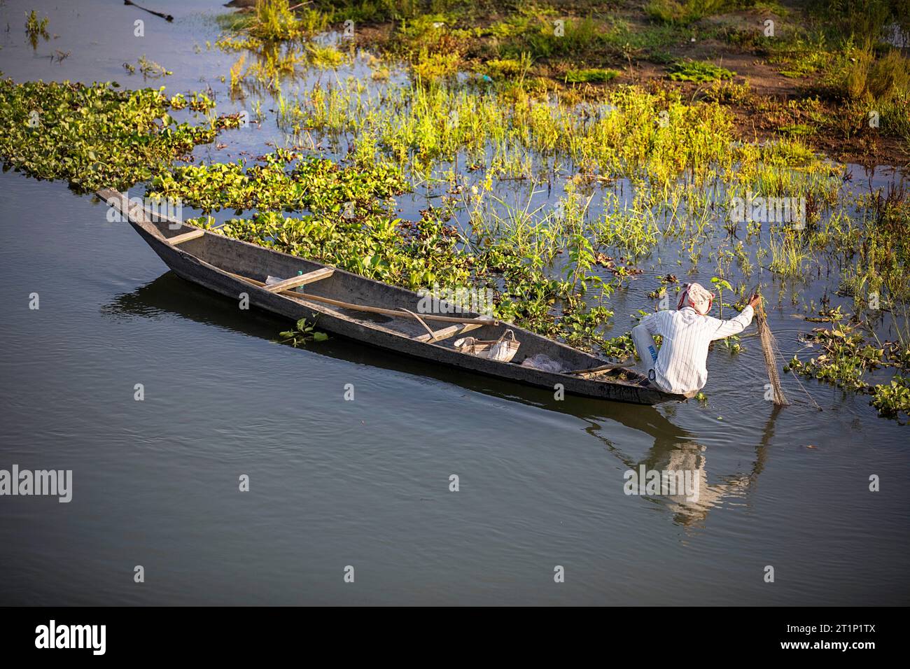 Local man fishing with a net from a wooden traditional boat on a river ...