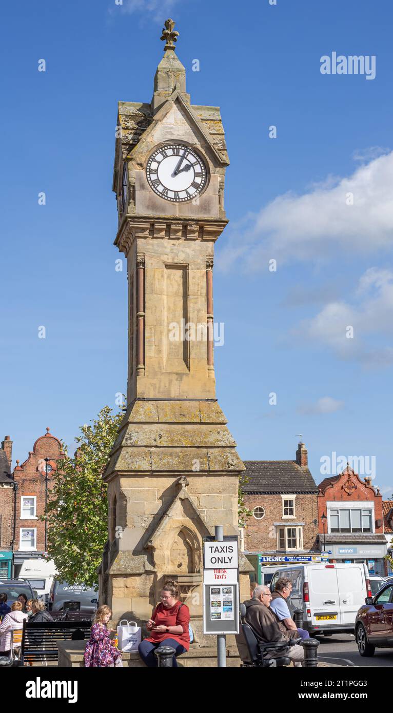 A clock tower in the market place of a country town. People sit at the ...