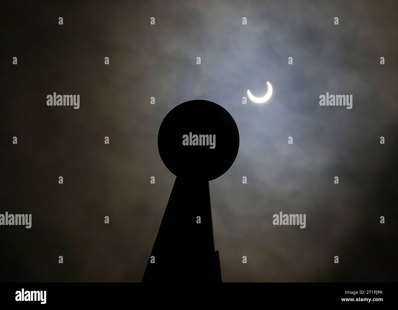 The sun, partially blocked clouds, is seen next to the top of a sundial ...