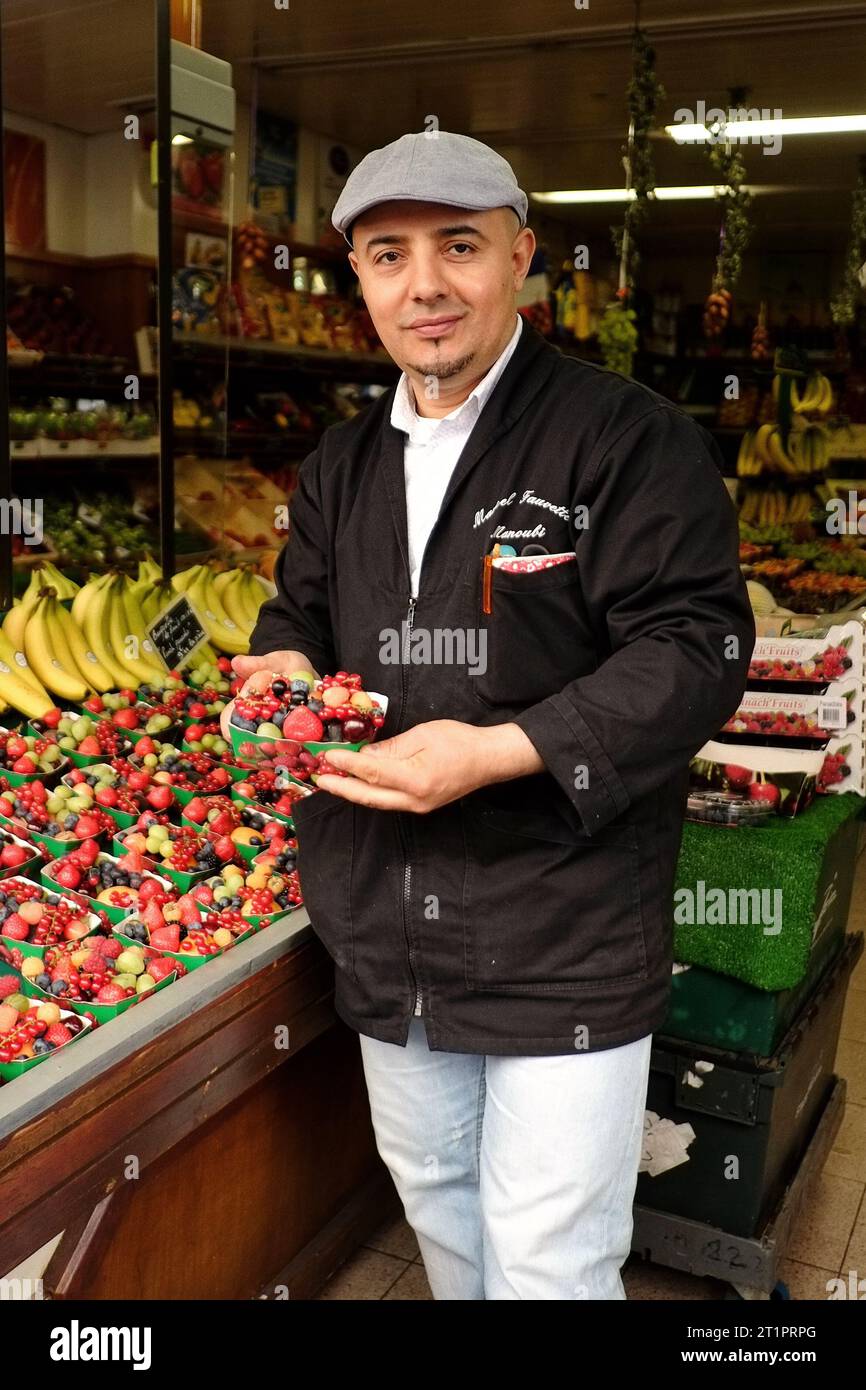 Portrait of a fruit seller holding a paper punnet of wild berries. Rows ...