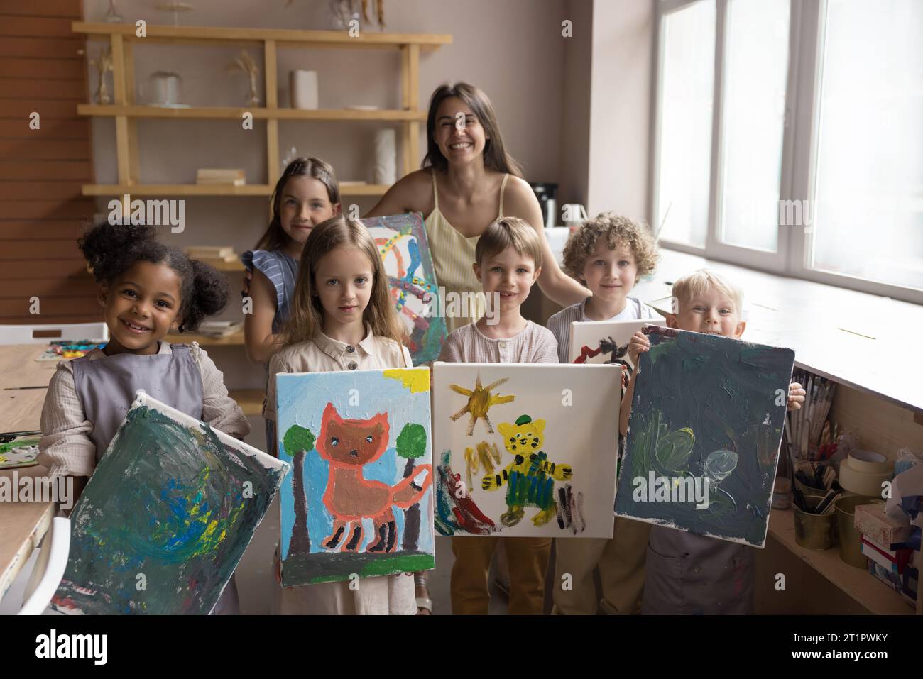 Children holding paintings posing in art studio with teacher Stock ...
