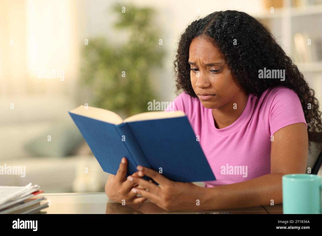 Sad black woman reading a book sitting at home Stock Photo - Alamy