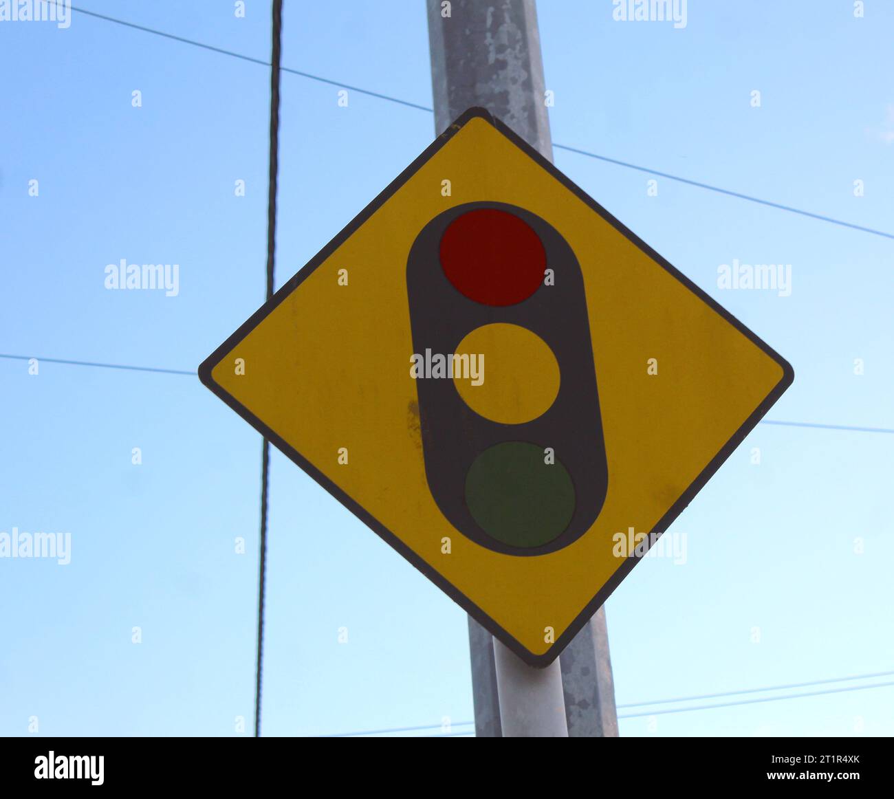 A photo of a yellow traffic light warning sign against a pale blue sky ...