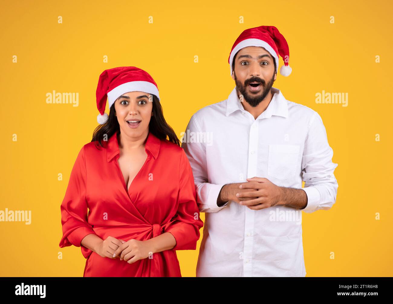 Happy shocked young couple in Christmas hats, isolated on yellow ...