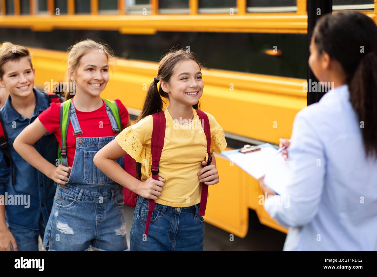 Happy children boarding school bus while black female teacher updating ...