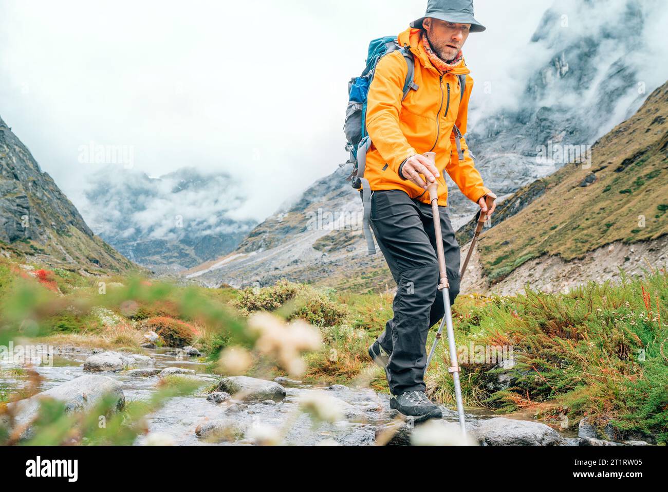 Man with backpack and trekking poles crossing mountain creek during ...