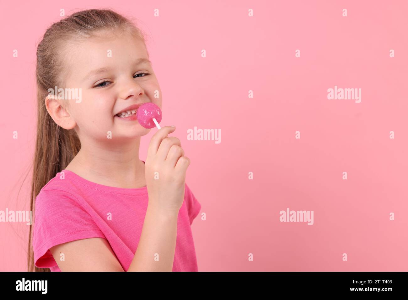 Happy little girl licking lollipop on pink background, space for text ...
