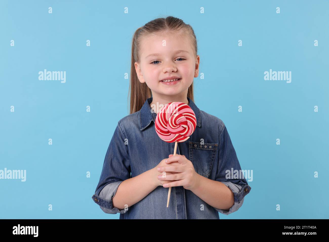 Happy little girl with bright lollipop swirl on light blue background ...
