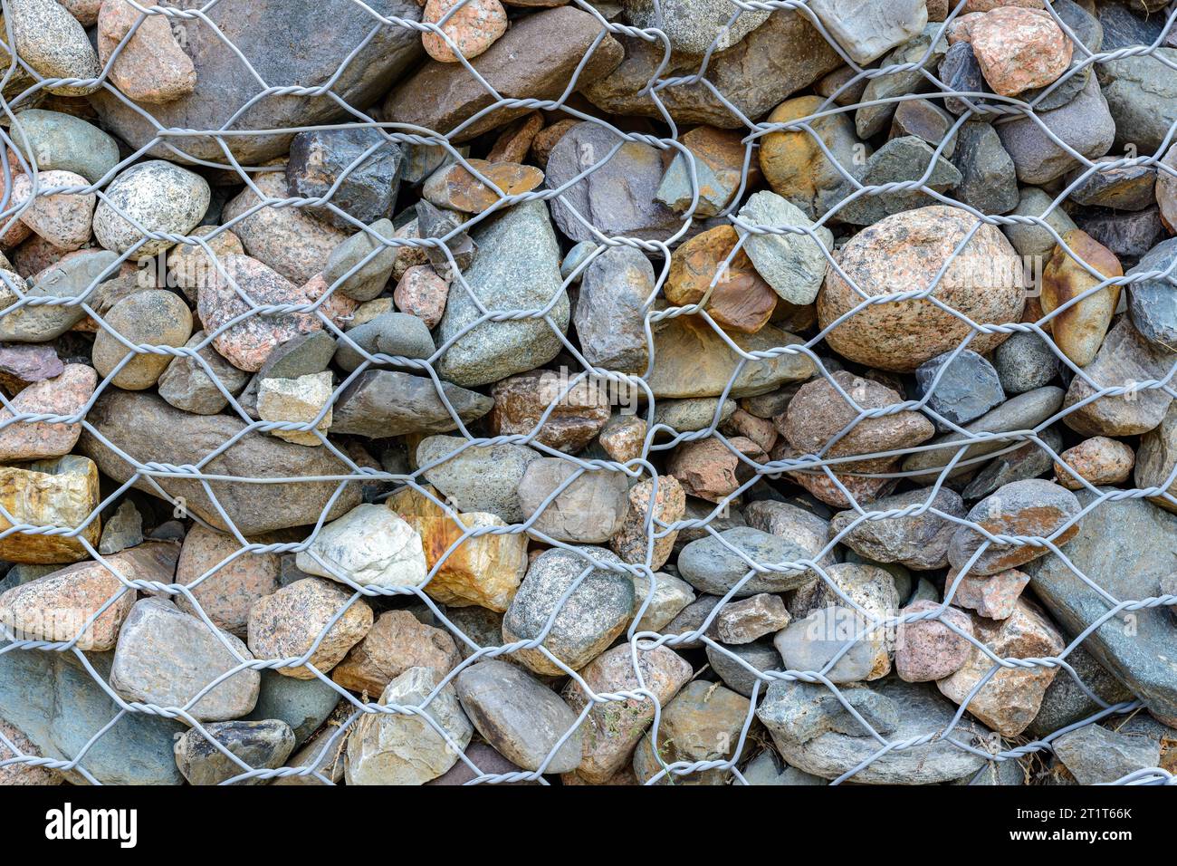 A closeup of a wire and rock retaining wall. The wire forms hex shaped ...