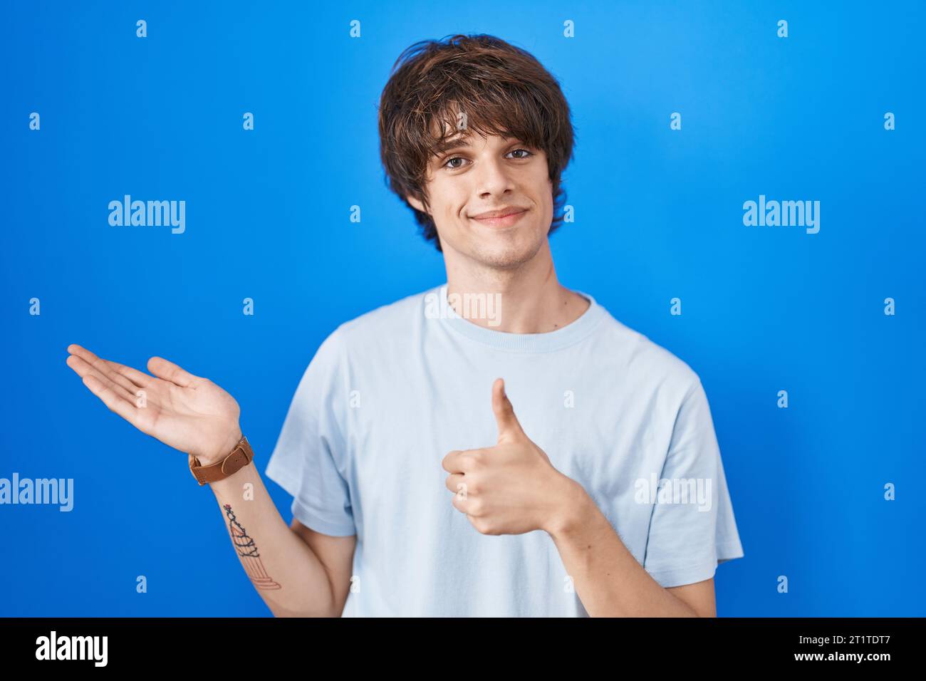 Hispanic young man standing over blue background showing palm hand and ...