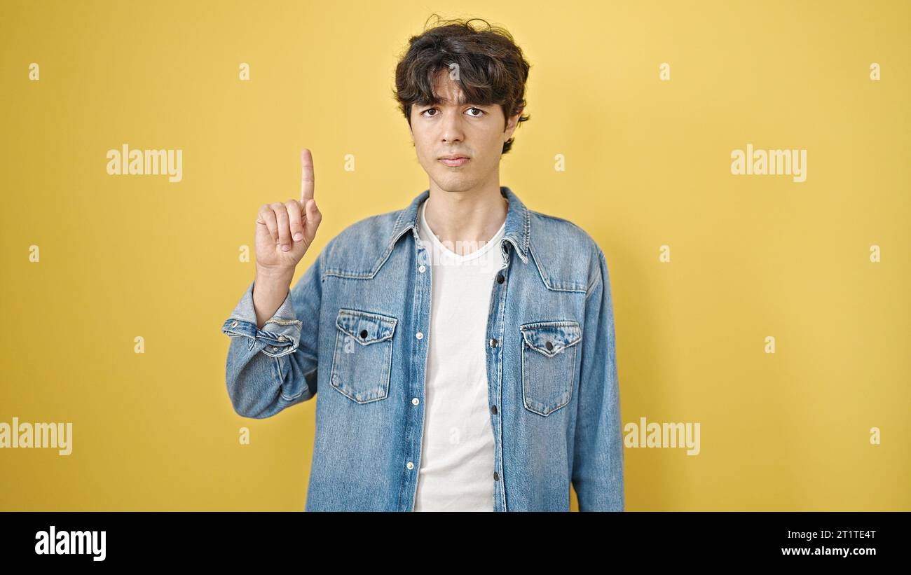 Young hispanic man saying no with finger over isolated yellow ...