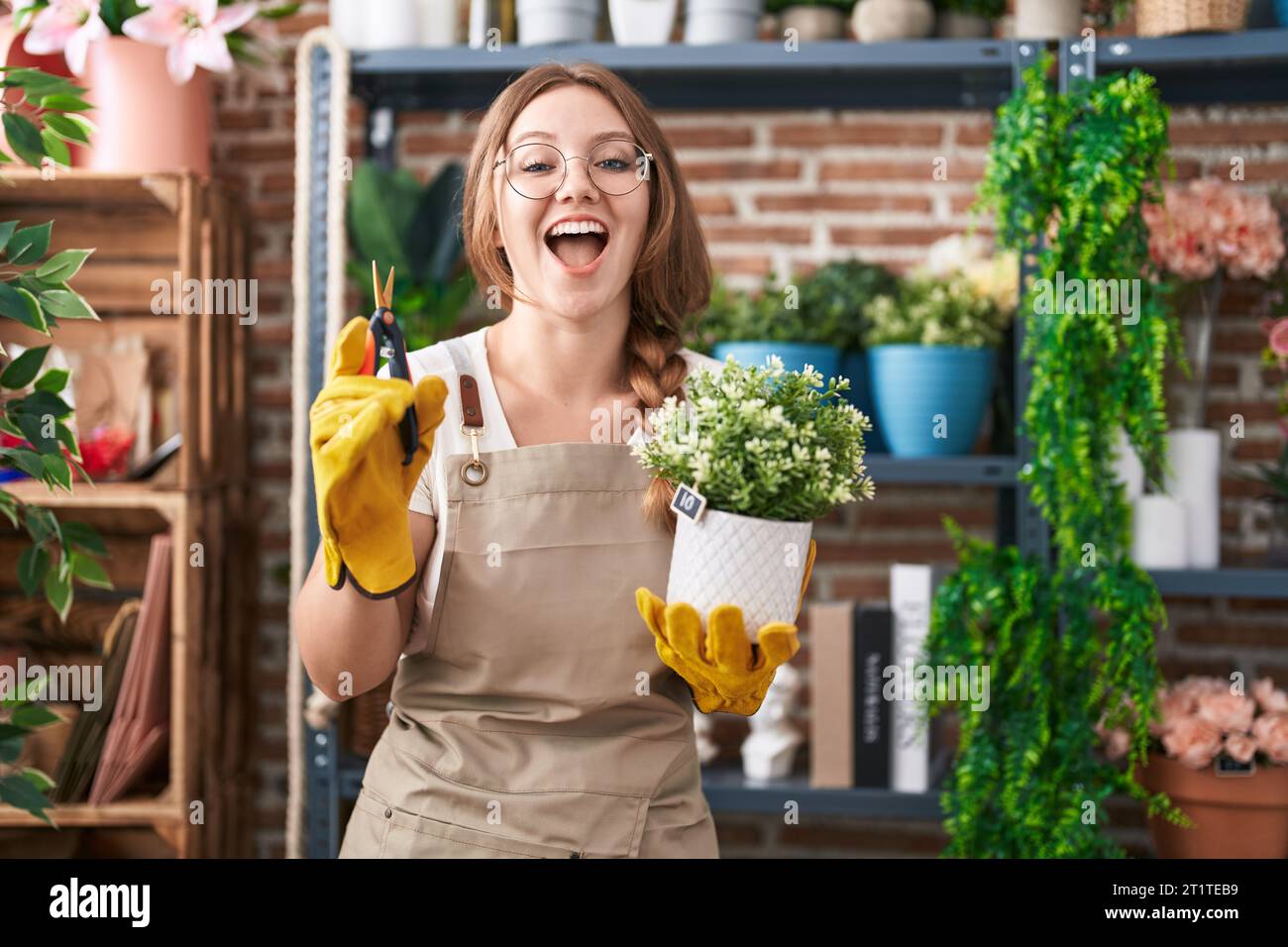 Young caucasian woman working at florist shop holding plant smiling and ...