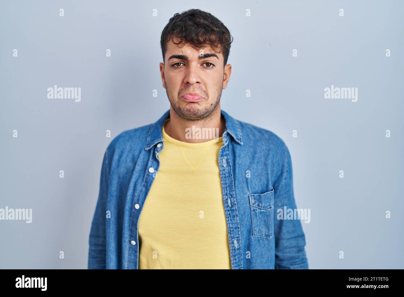 Young hispanic man standing over blue background depressed and worry ...