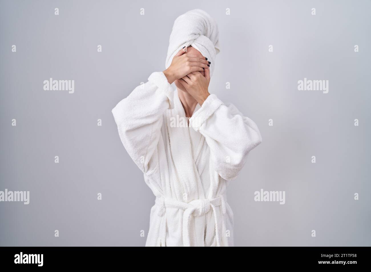 Blonde caucasian woman wearing bathrobe covering eyes and mouth with ...