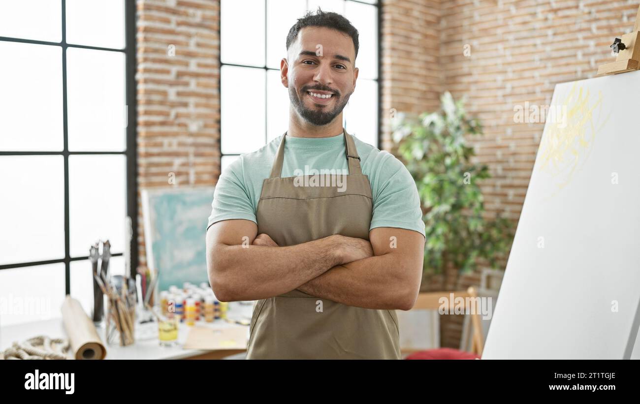 Young arab man artist standing with arms crossed gesture smiling at art ...