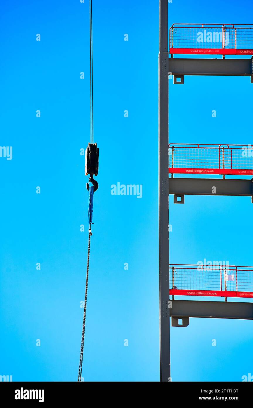 Crane hook and skeleton of building under construction set against blue ...
