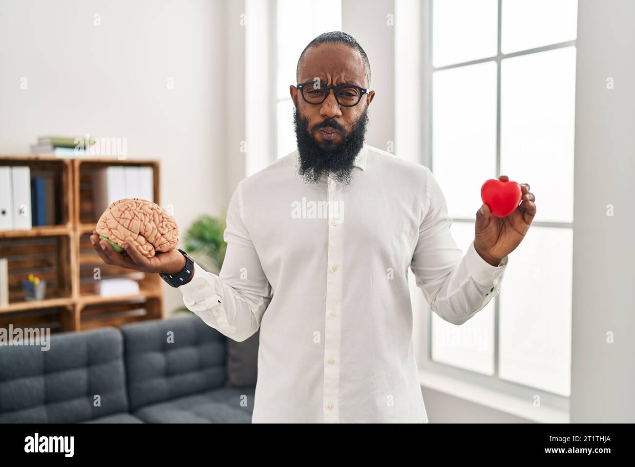 African american man working at therapy office holding brain and heart ...