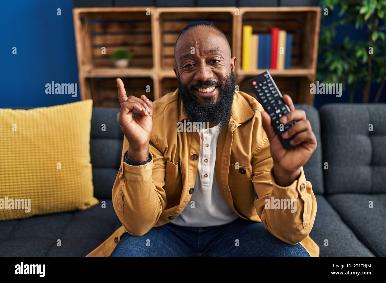 African american man holding television remote control smiling happy ...