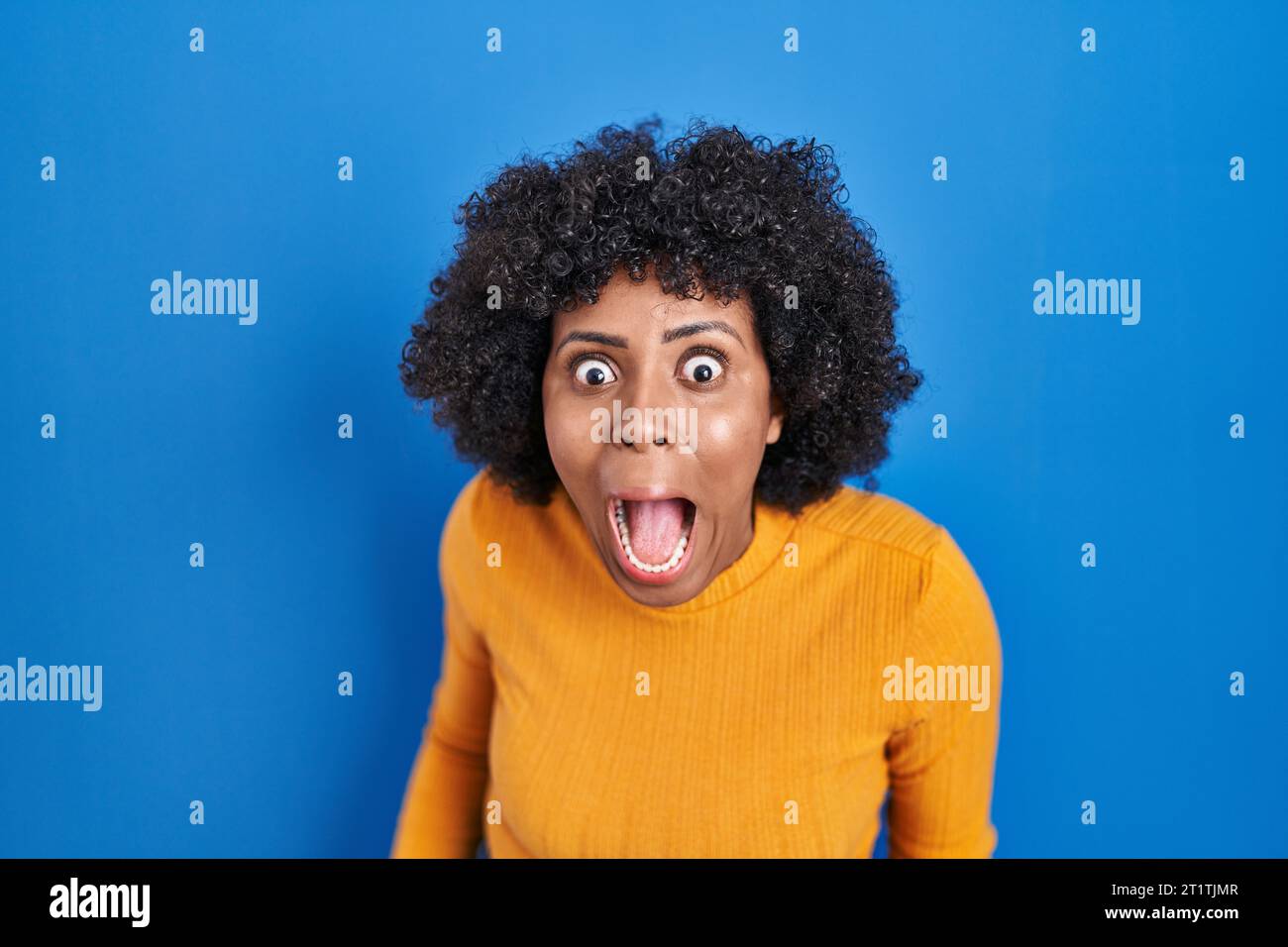Black woman with curly hair standing over blue background angry and mad ...