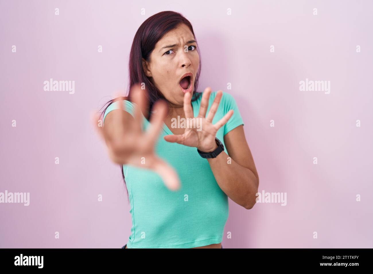 Young hispanic woman standing over pink background afraid and terrified ...