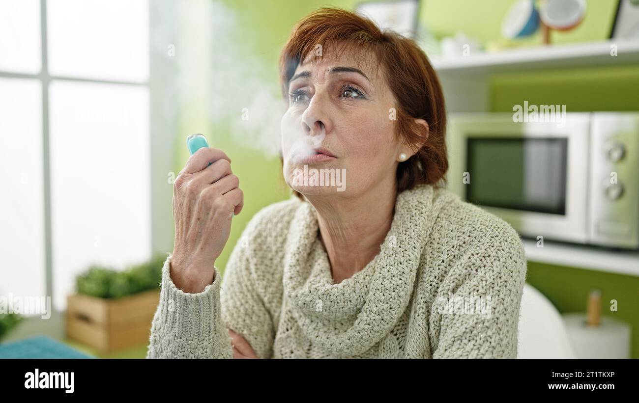 Mature hispanic woman vaping sitting on table at dinning room Stock ...