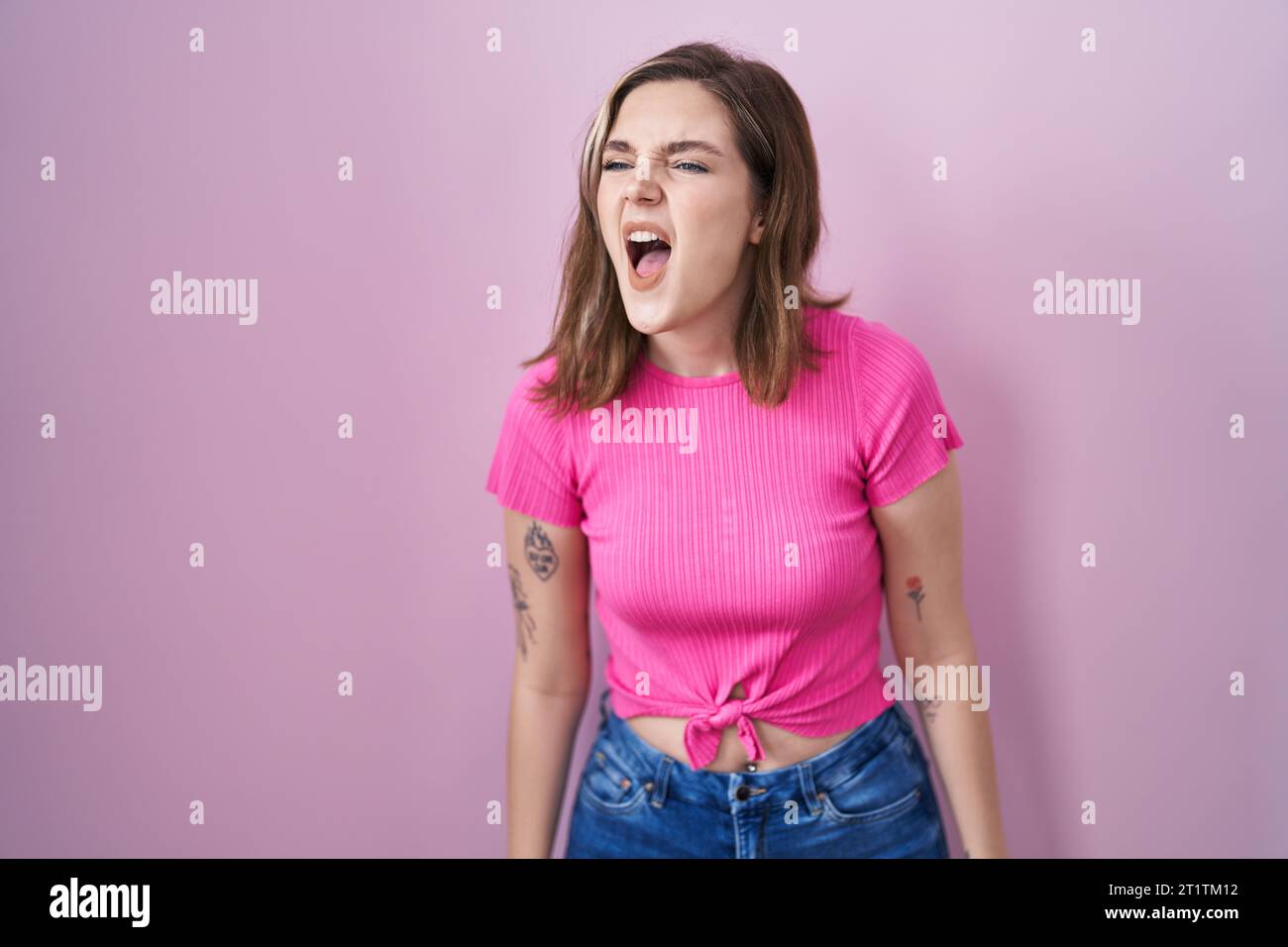 Blonde caucasian woman standing over pink background angry and mad ...
