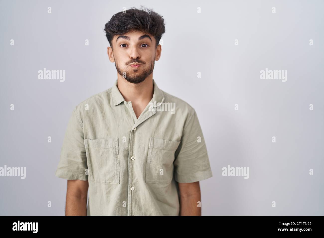 Arab man with beard standing over white background puffing cheeks with ...