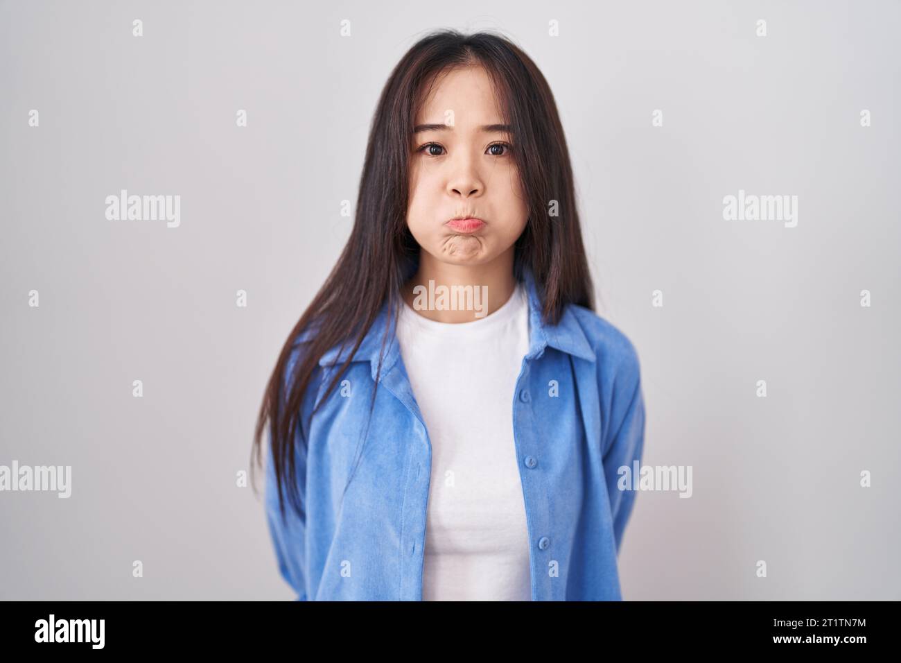 Young chinese woman standing over white background puffing cheeks with ...