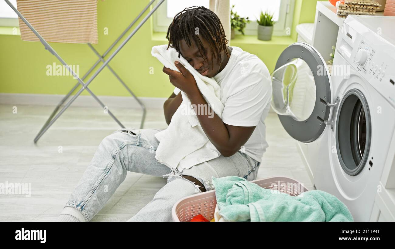 African american man smelling clean clothes smiling at laundry room ...