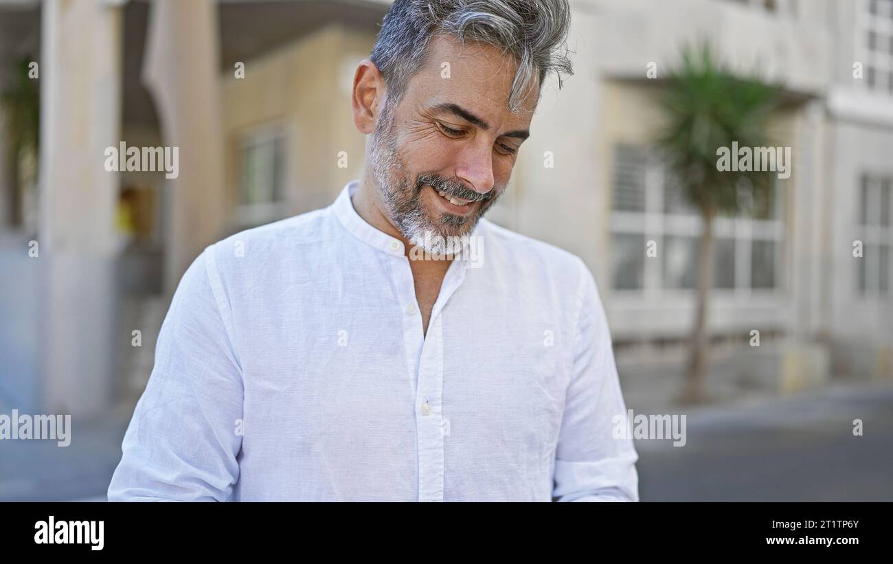 Young grey-haired hispanic man, confidently smiling, standing, basking ...
