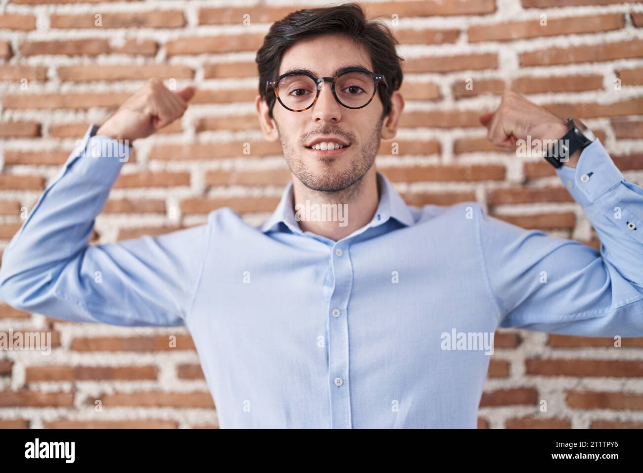 Young hispanic man standing over brick wall background showing arms ...