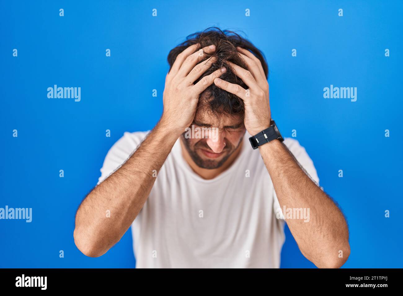 Hispanic young man standing over blue background suffering from ...