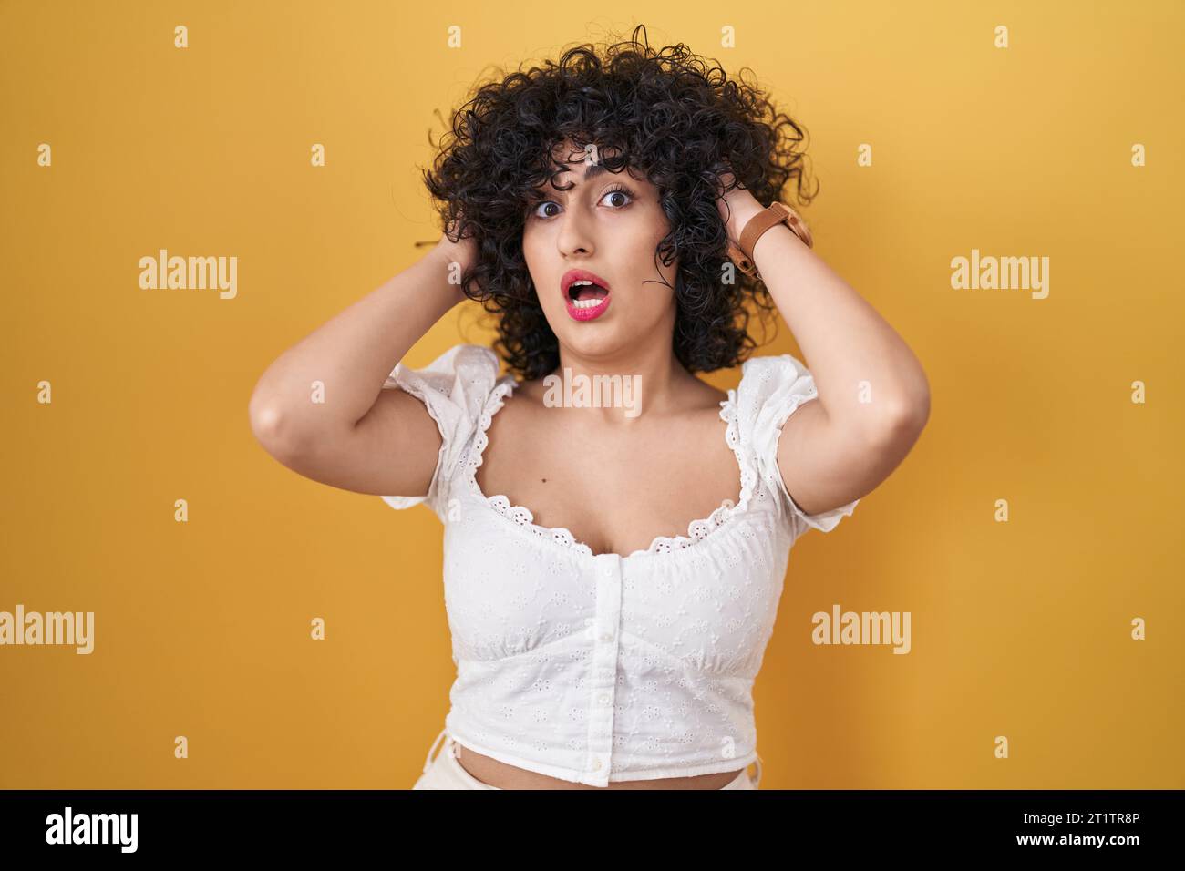 Young brunette woman with curly hair standing over yellow background ...
