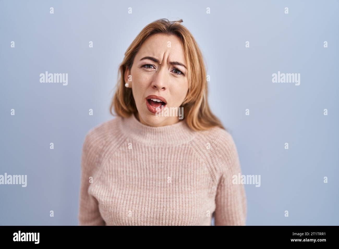 Hispanic woman standing over blue background in shock face, looking ...